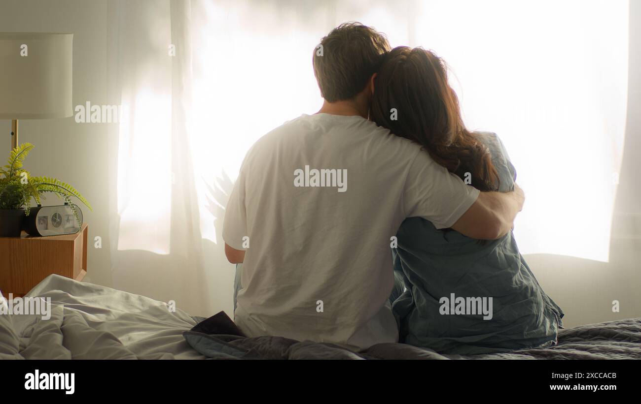 Back view man woman sitting on bed boyfriend hug girlfriend together ...
