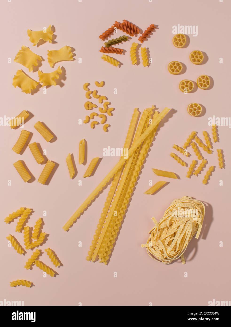 Assorted uncooked pasta varieties arranged on a pink background ...