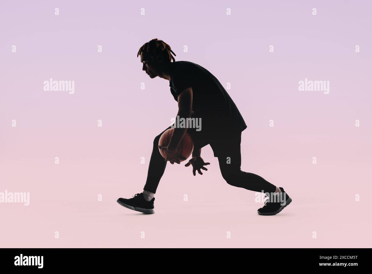 Silhouetted against a pink background, a young male basketball player ...