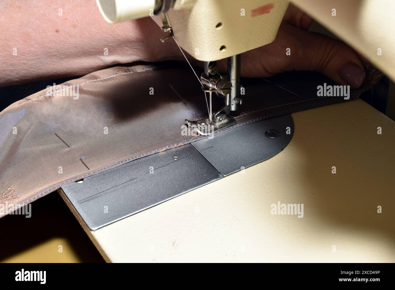 A seamstress works at a sewing machine while sitting at a table, she ...