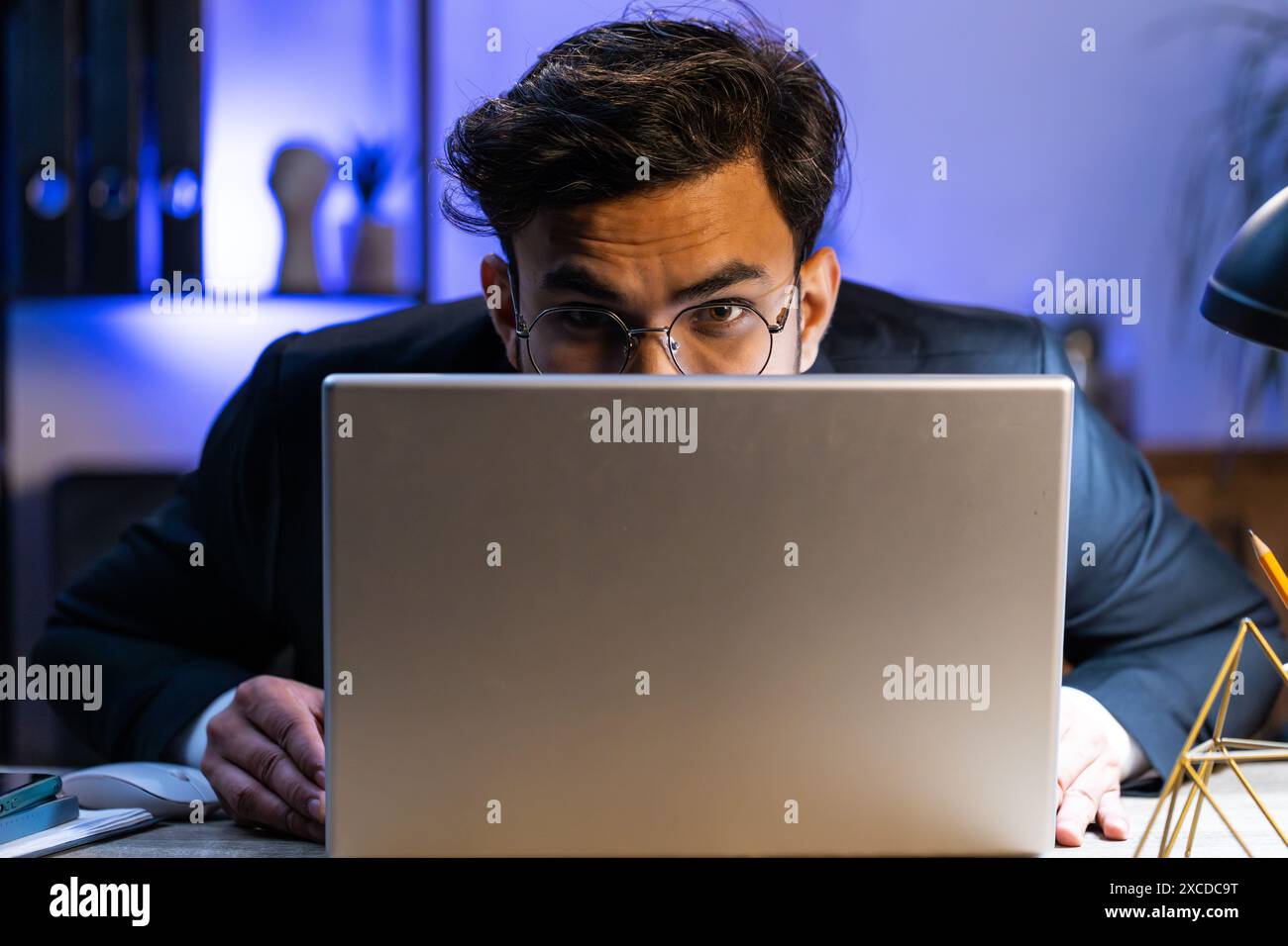 Confident Indian businessman hiding behind laptop computer, looking at ...