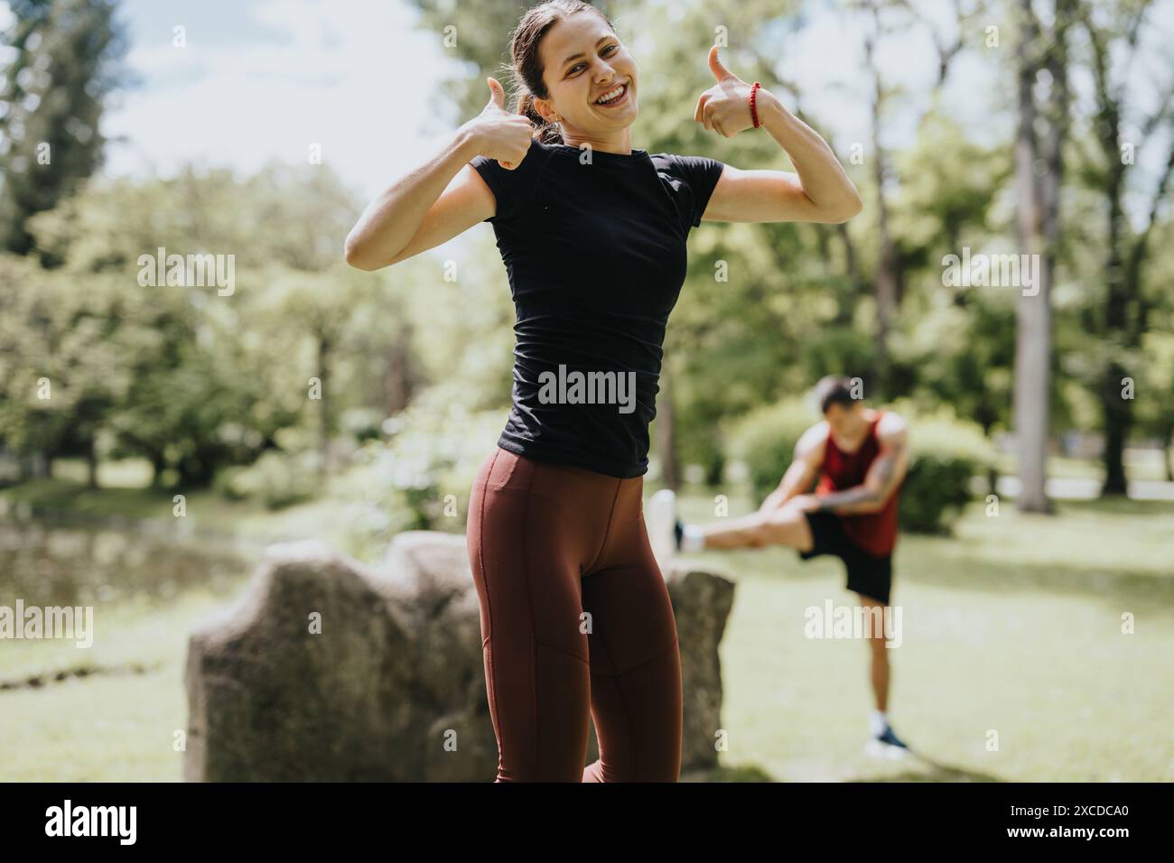 Smiling woman giving thumbs up while exercising in park with friend ...