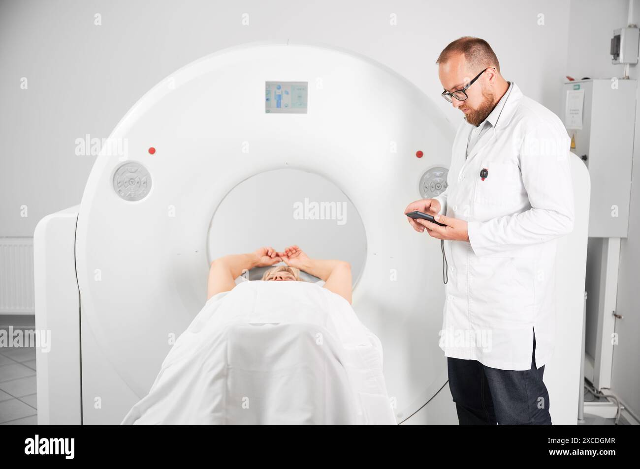 Medical computed tomography or MRI scanner. Doctor holding mobile phone and examining results of ...