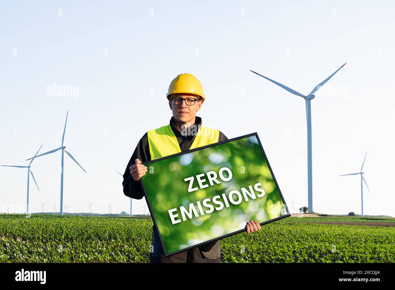 Worker in helmet holds board with text ZERO EMISSION on a field of wind turbines Stock Photo - Alamy