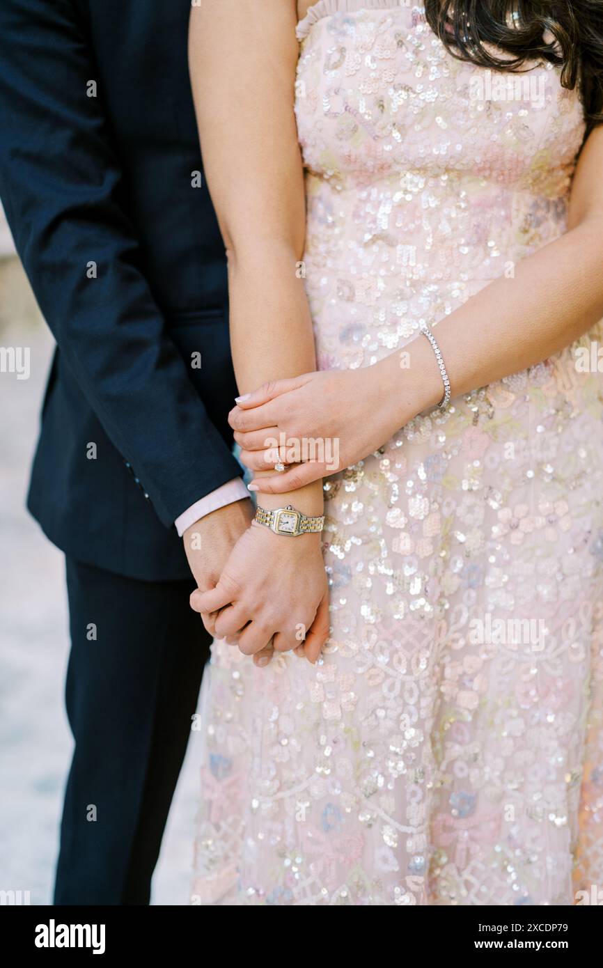 Bride holds the hand of groom standing behind her, placing her palm on ...