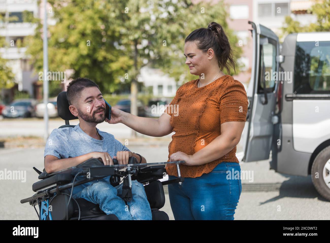 Female assistant helping a man in a wheelchair to use a smartphone ...