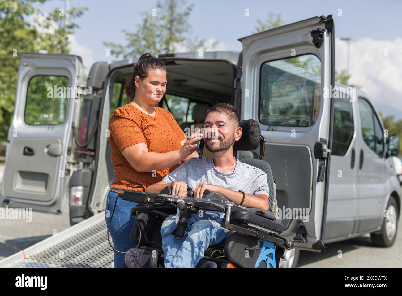 Female assistant helping a man in a wheelchair to use a smartphone ...