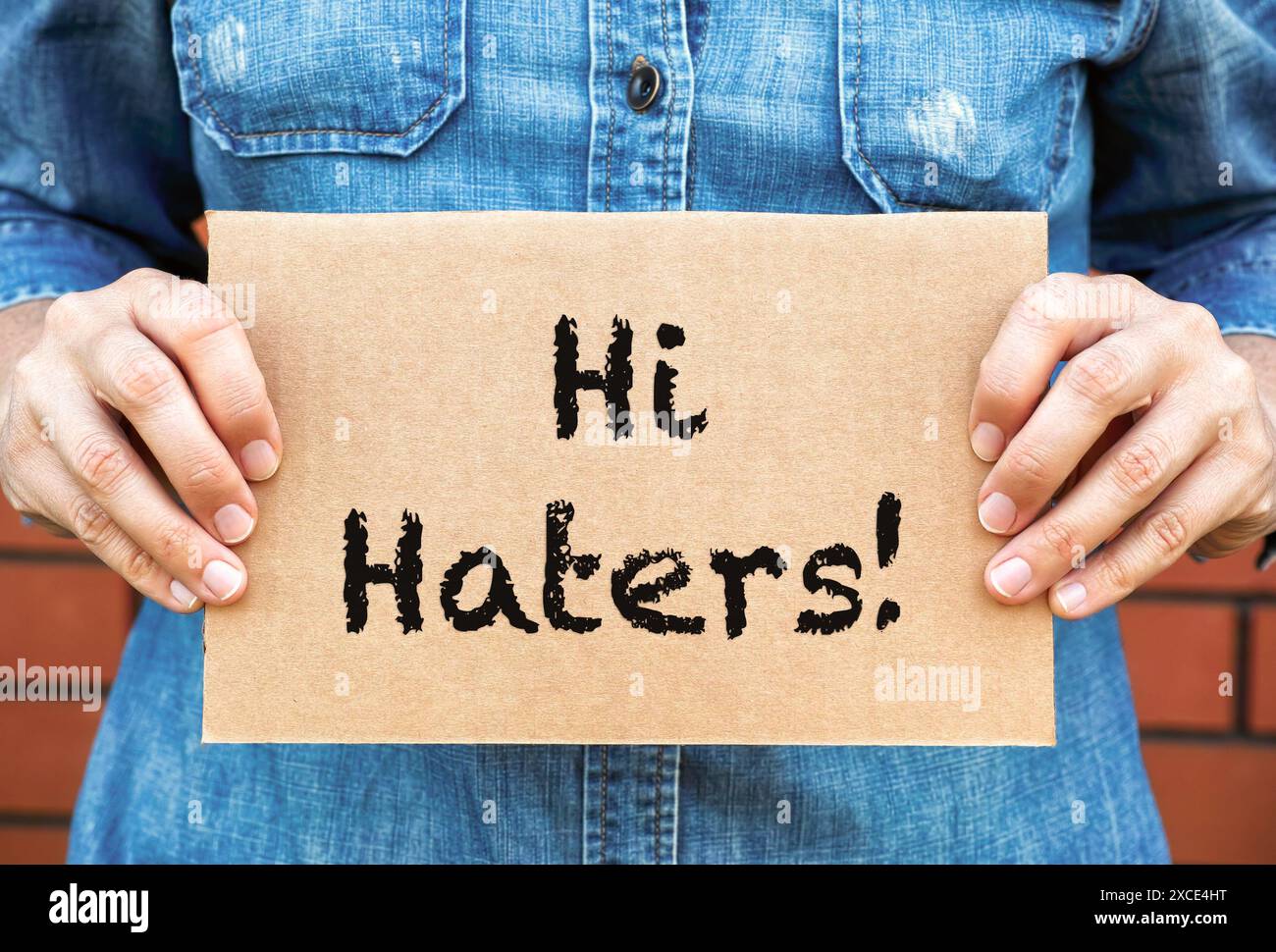 Woman holding a piece of a cardboard with words Hi Haters against brick ...