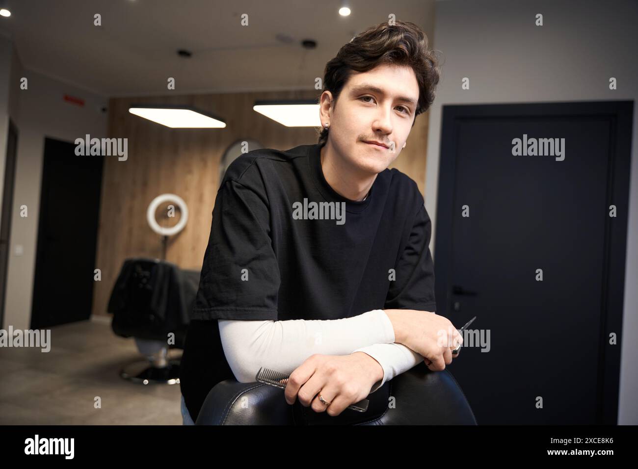 Diligent barber posing at camera in contemporary hairdressing salon ...