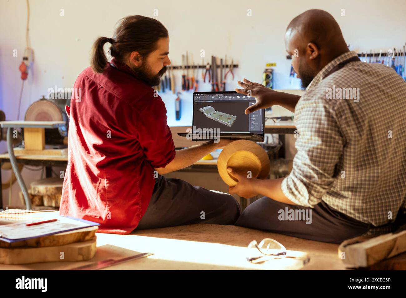 BIPOC artisan and apprentice comparing wood art piece with schematic displayed on CAD software ...