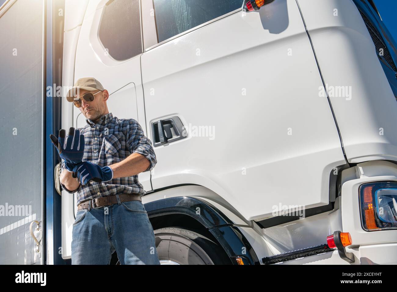 A truck driver, wearing a plaid shirt and a baseball cap, is putting on ...