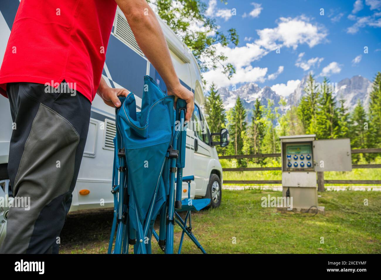 A man sets up a folding chair outside of a white campervan, preparing ...