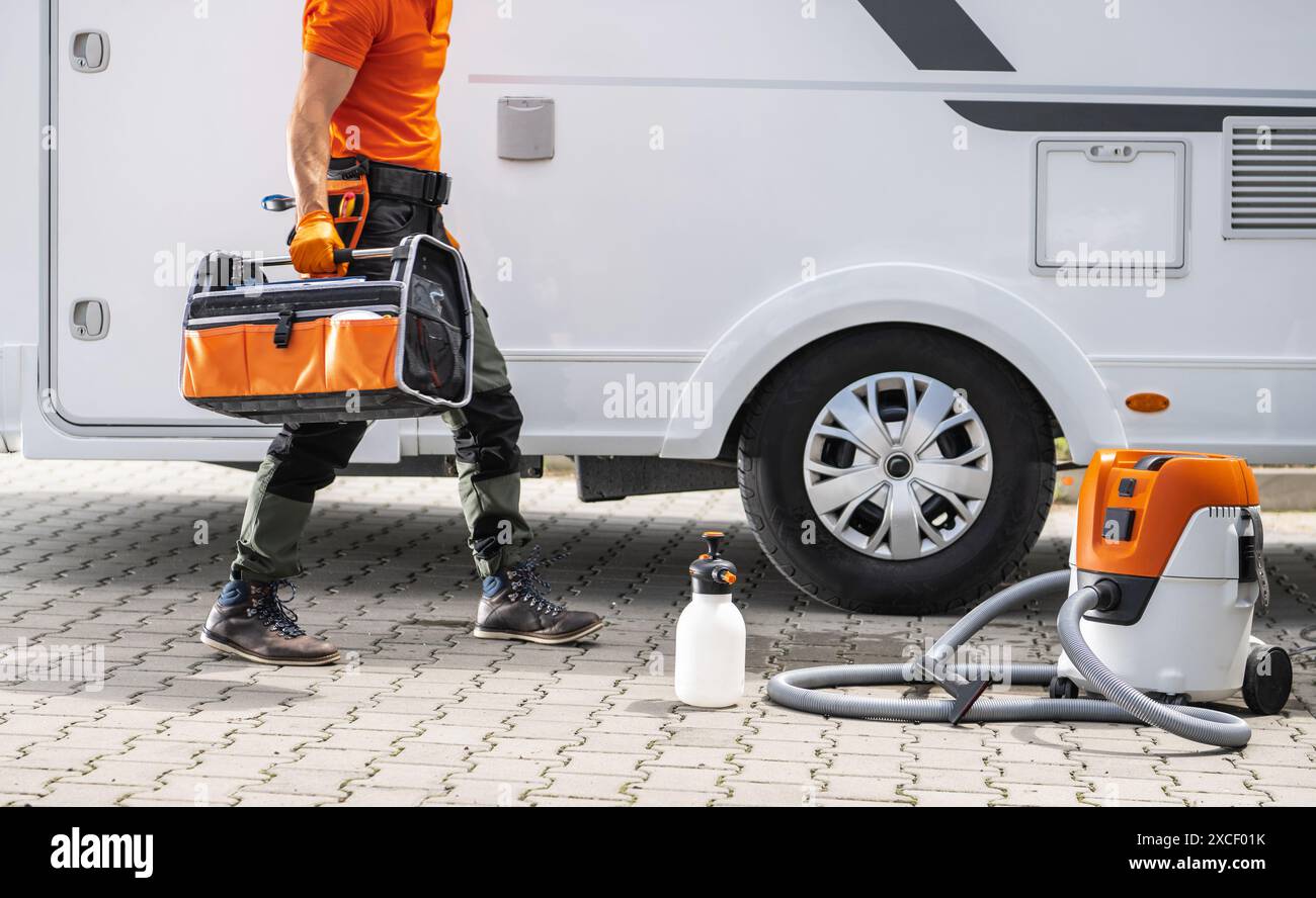 RV technician walks toward a white camper van, carrying a toolbox. He ...