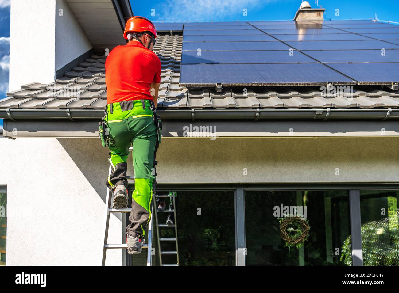 A worker wearing a hard hat and safety gear is climbing a ladder to ...