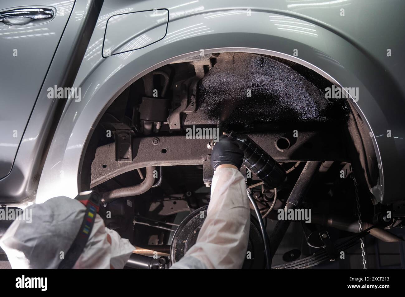 An auto mechanic applies anti-corrosion mastic to the underbody of a ...