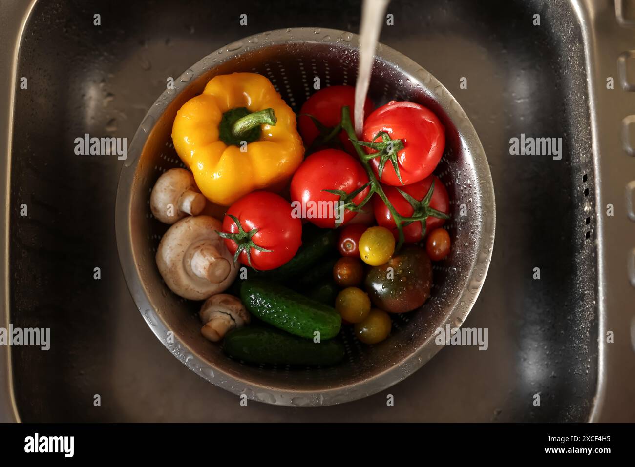 Washing different vegetables with tap water in metal colander inside ...