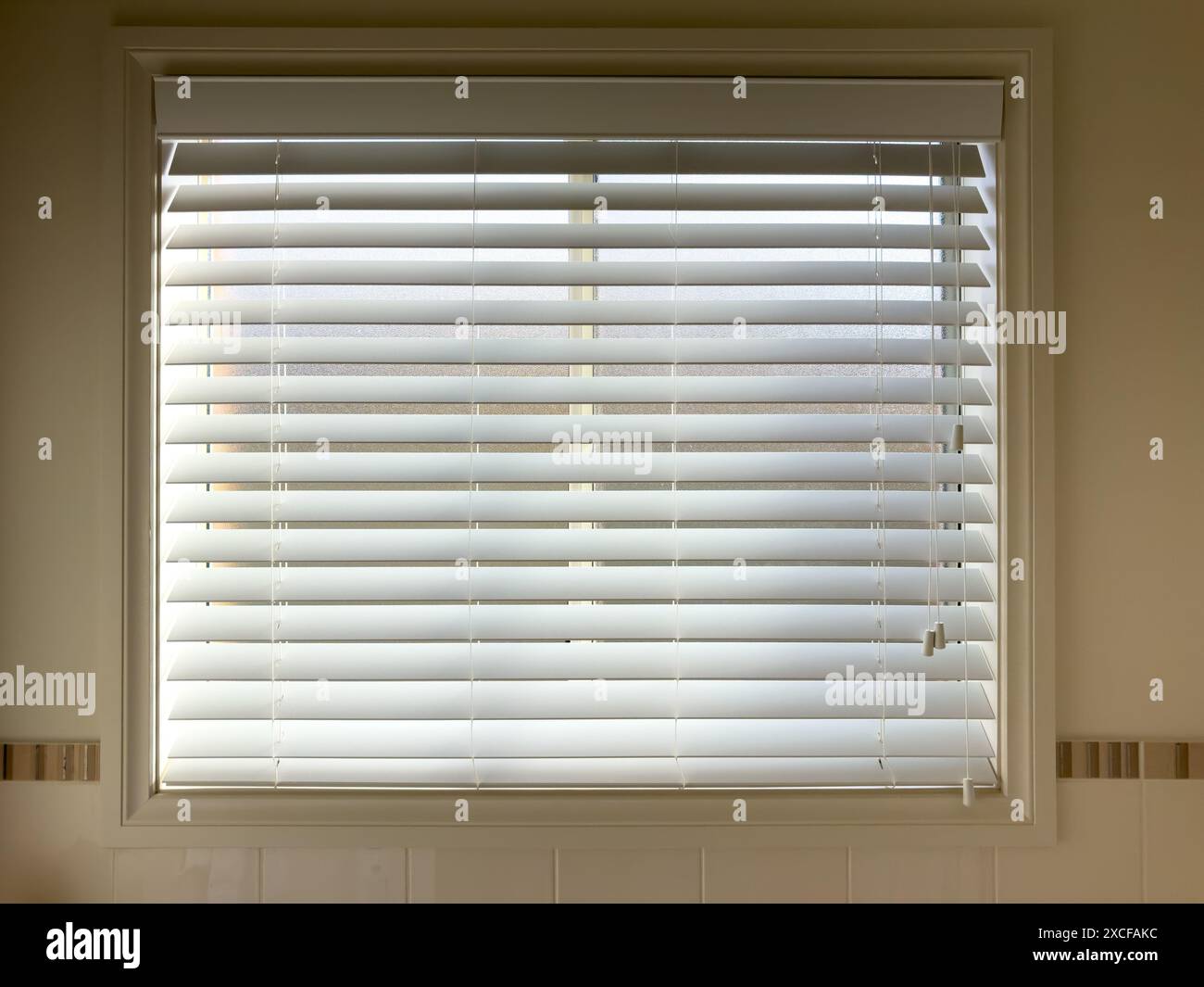 White wooden window blinds partially open with adjustment cords inside ...
