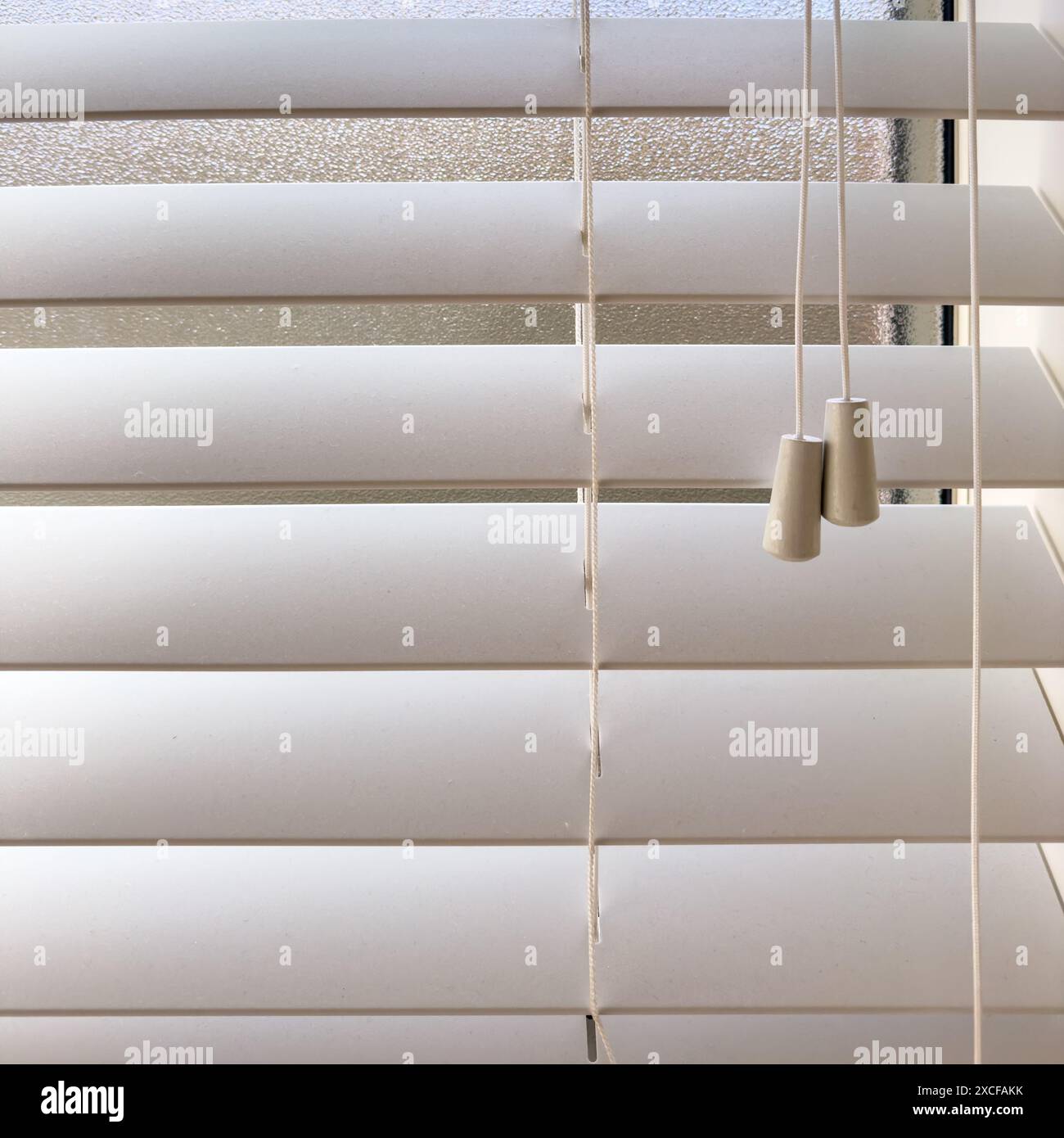 White wooden window blinds partially open with adjustment cords inside ...