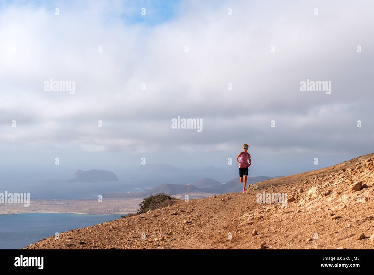 Woman jogging on a mountain trail overlooking the ocean with beautiful ...