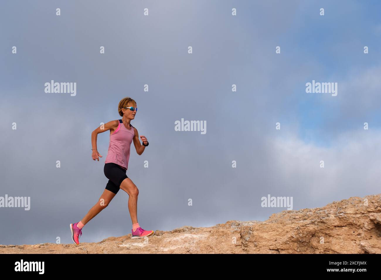 Woman running uphill on rocky terrain under a cloudy sky, conveying ...