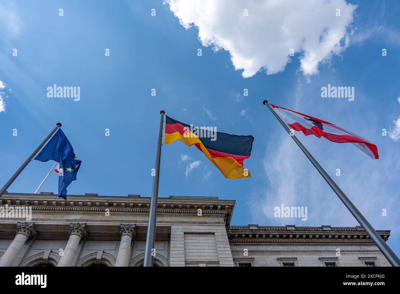 Three flags are flying on poles outside a building. The flags are of ...