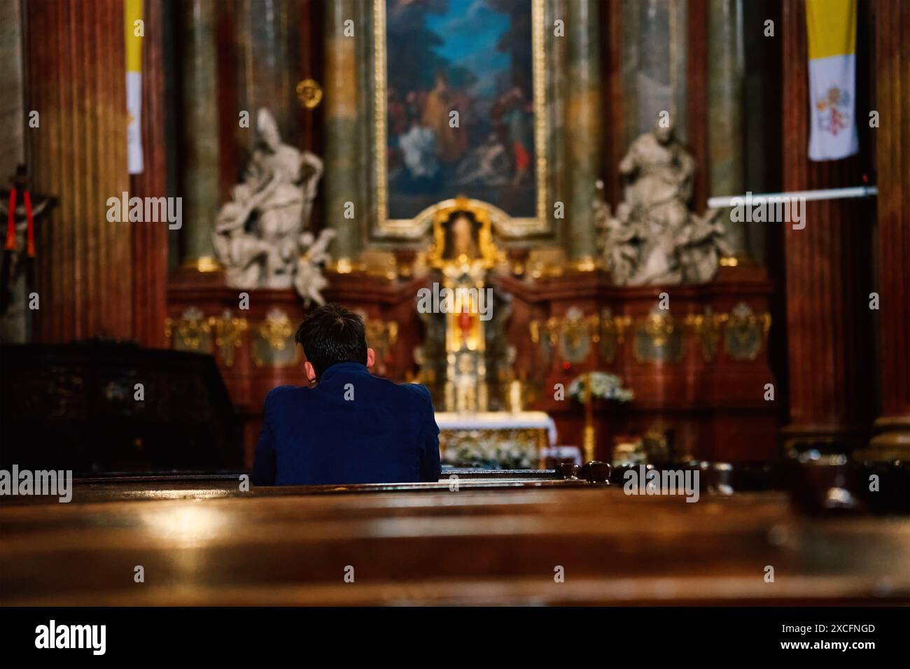 Back view of man in blue jacket prays in catholic church. He is seated ...