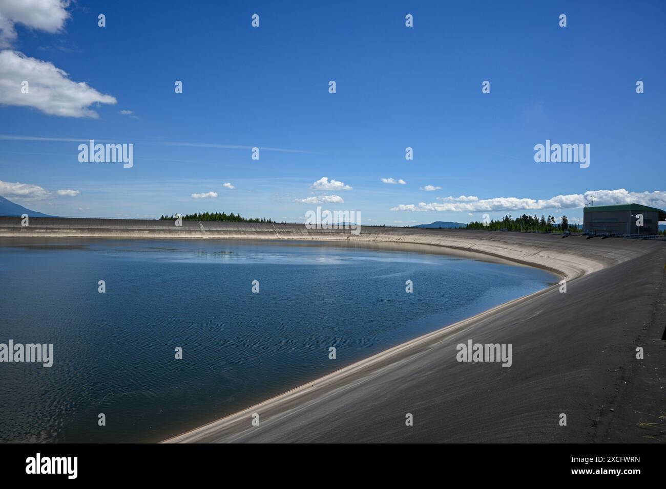 Water reservoir with dam wall and building on a sunny day with blue sky ...