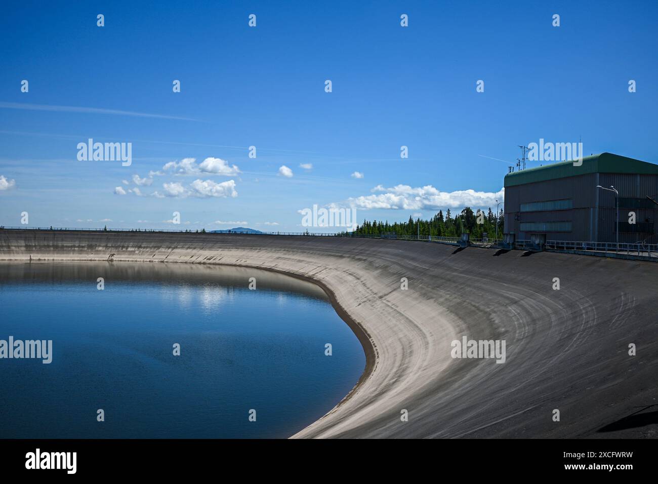 Water reservoir with dam wall and building on a sunny day with blue sky ...