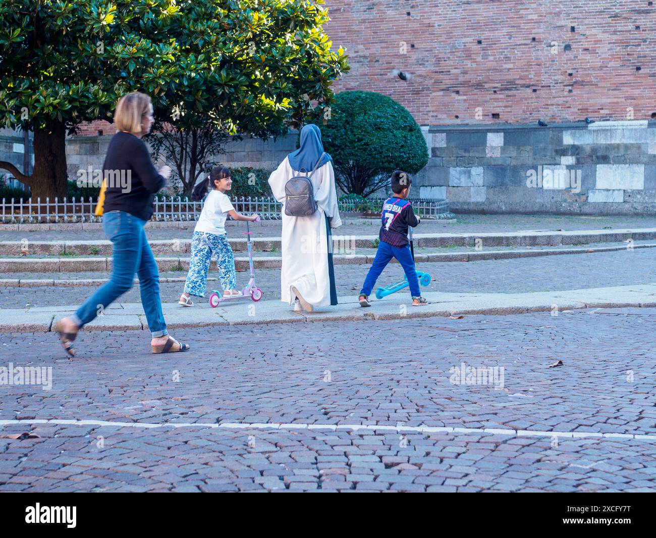 Cremona, Italy - June 10th 2024 Nun, children riding scooters, and a ...