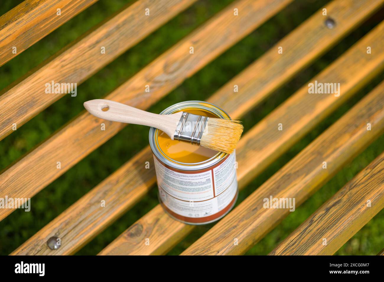 Brush and open can of paint on a wooden bench outdoors. The paint is a ...