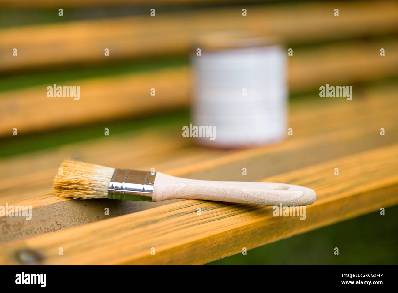 Brush and open can of paint on a wooden bench outdoors. The paint is a ...
