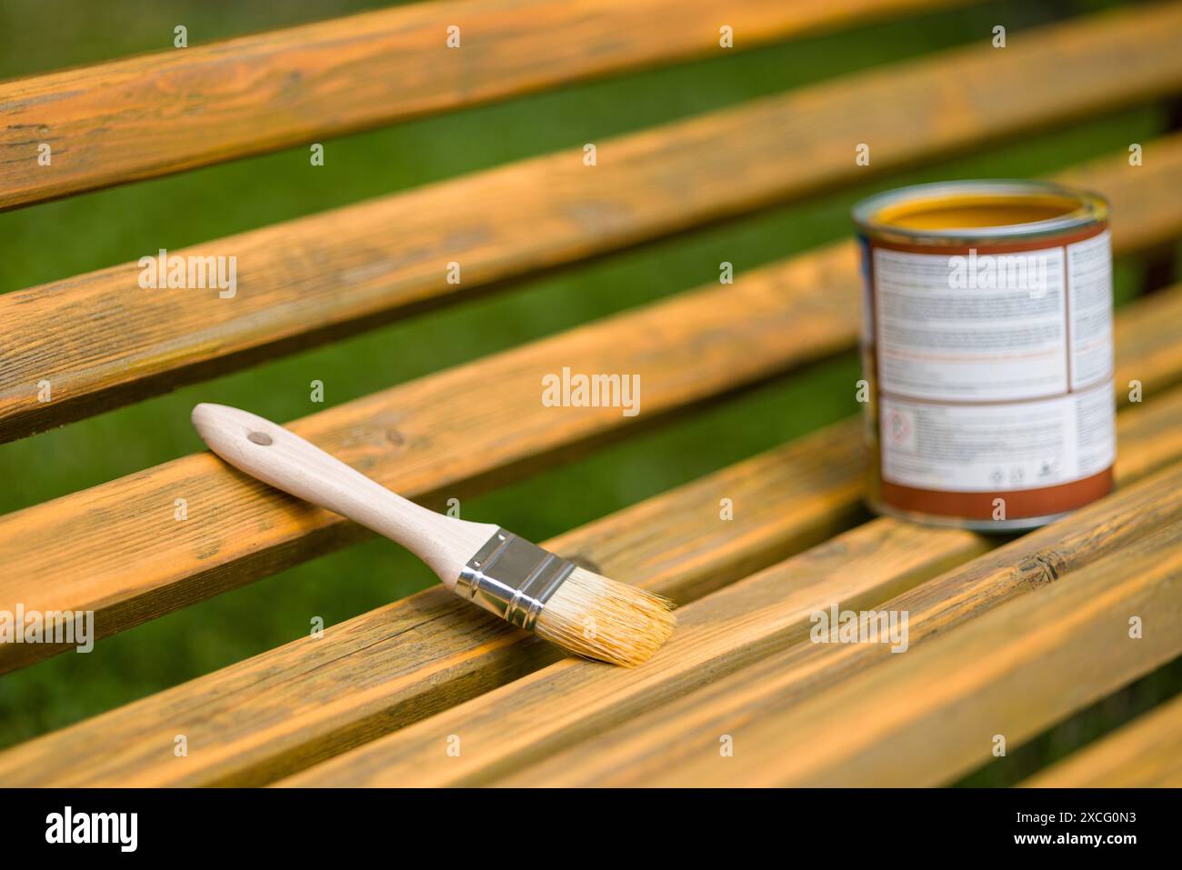 Brush and open can of paint on a wooden bench outdoors. The paint is a ...