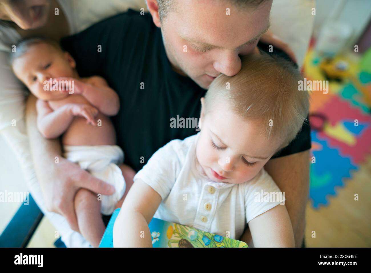 Father holding newborn baby daughter, while reading book with older son ...