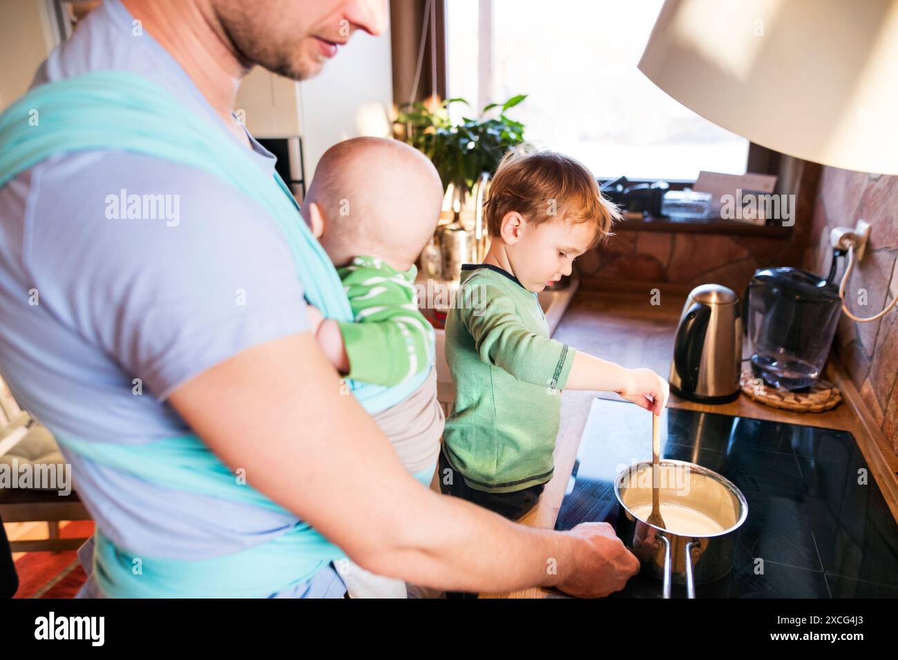 Father holding small baby in baby sling. Older brother stirring ...