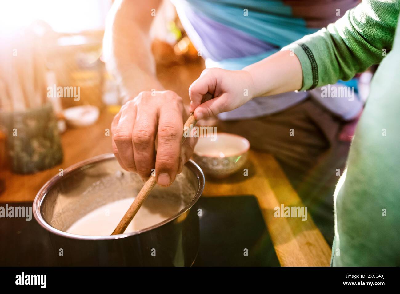 Father holding small baby in baby sling. Older brother stirring ...