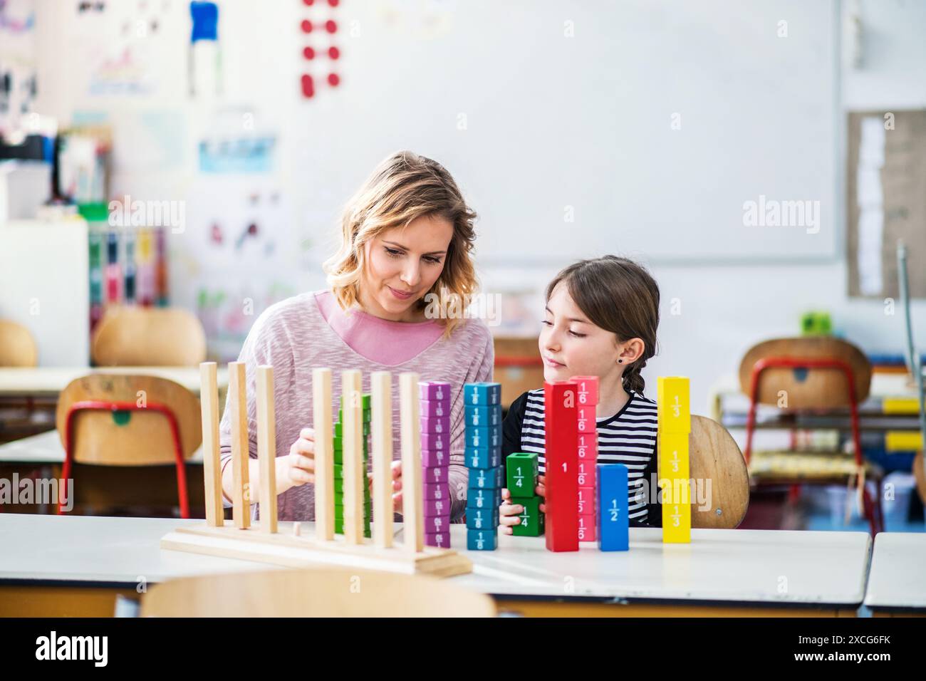 Hardworking teacher learning with young schoolgirl in classroom ...
