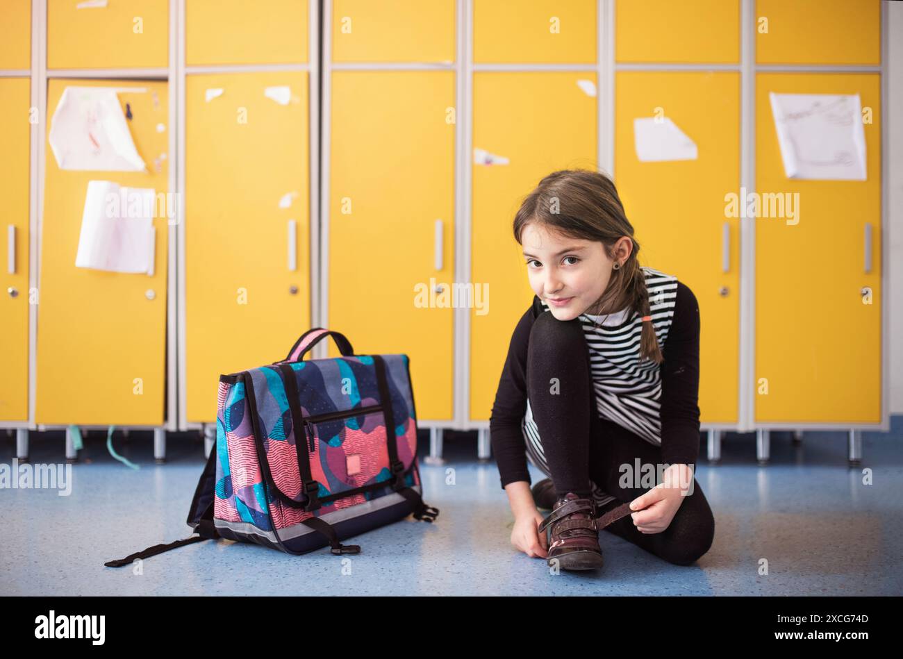 Portrait of cute schoolgirl, putting shoes on by lockers. Student girl ...