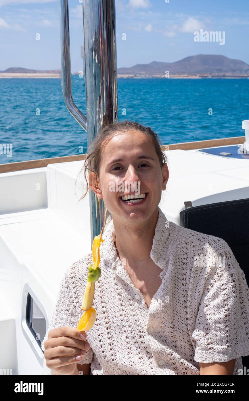 A young man smiles brightly while enjoying a snack on a boat, the vast ...