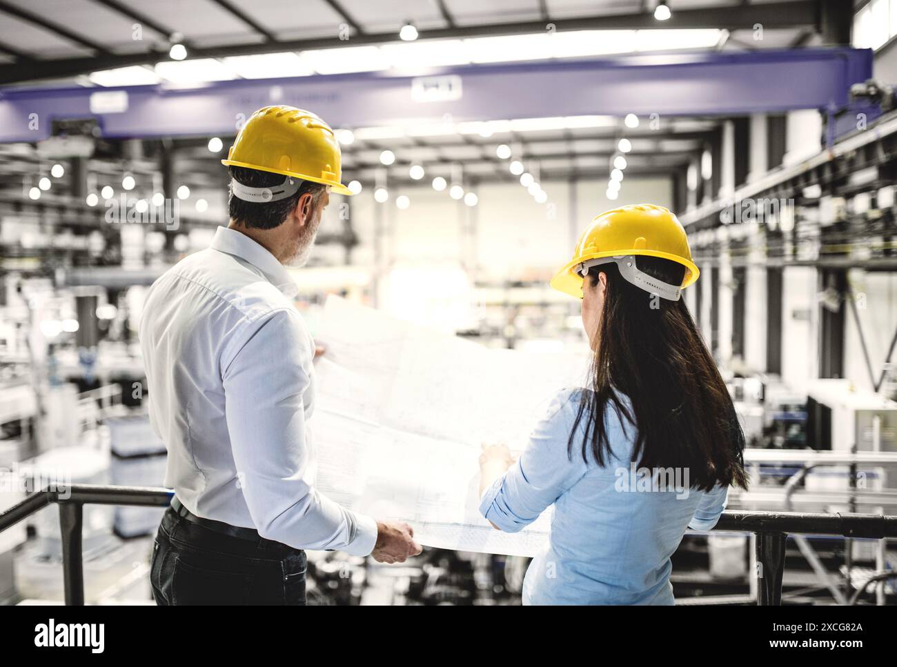 Two project managers standing in modern industrial factory, looking ...