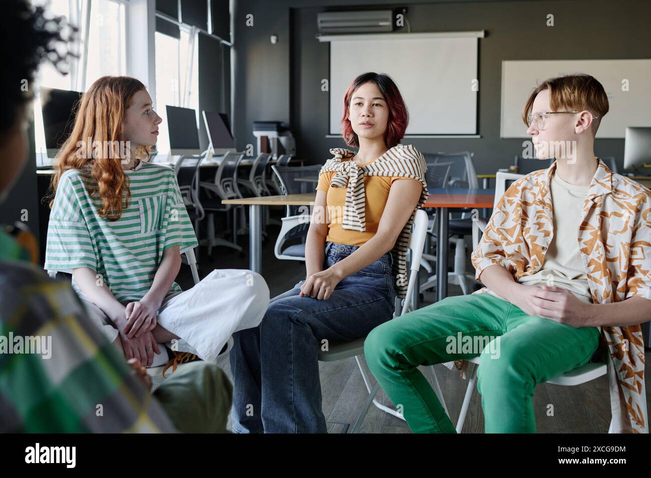 Asian teen girl sitting on chair speaking about her problems during group therapy session at ...