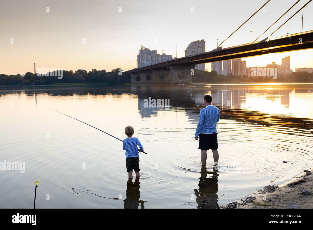 Dad and son fish together, standing with their backs with fishing rods ...