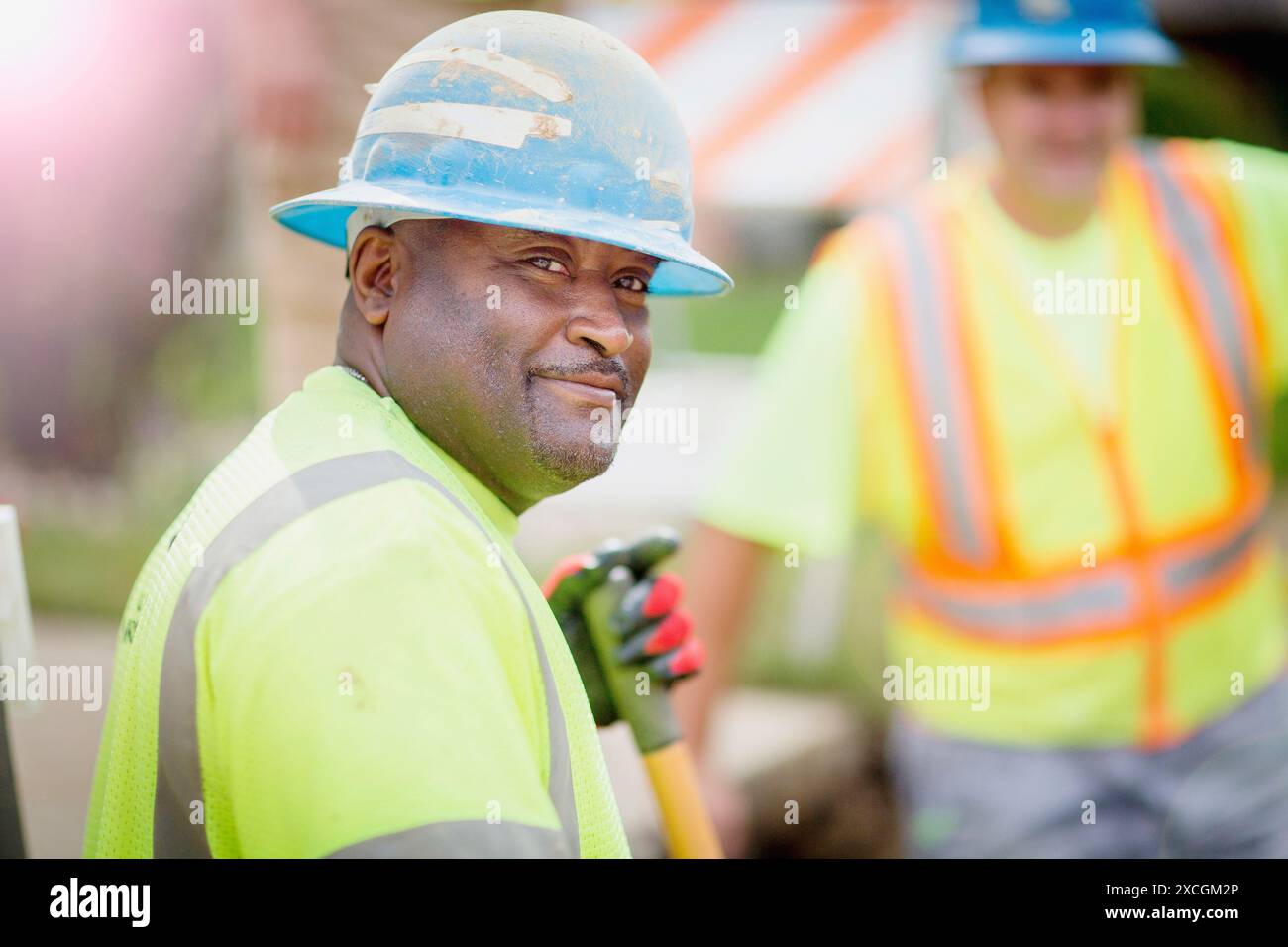 A utility worker in full uniform and helmet on poses with a work tool ...