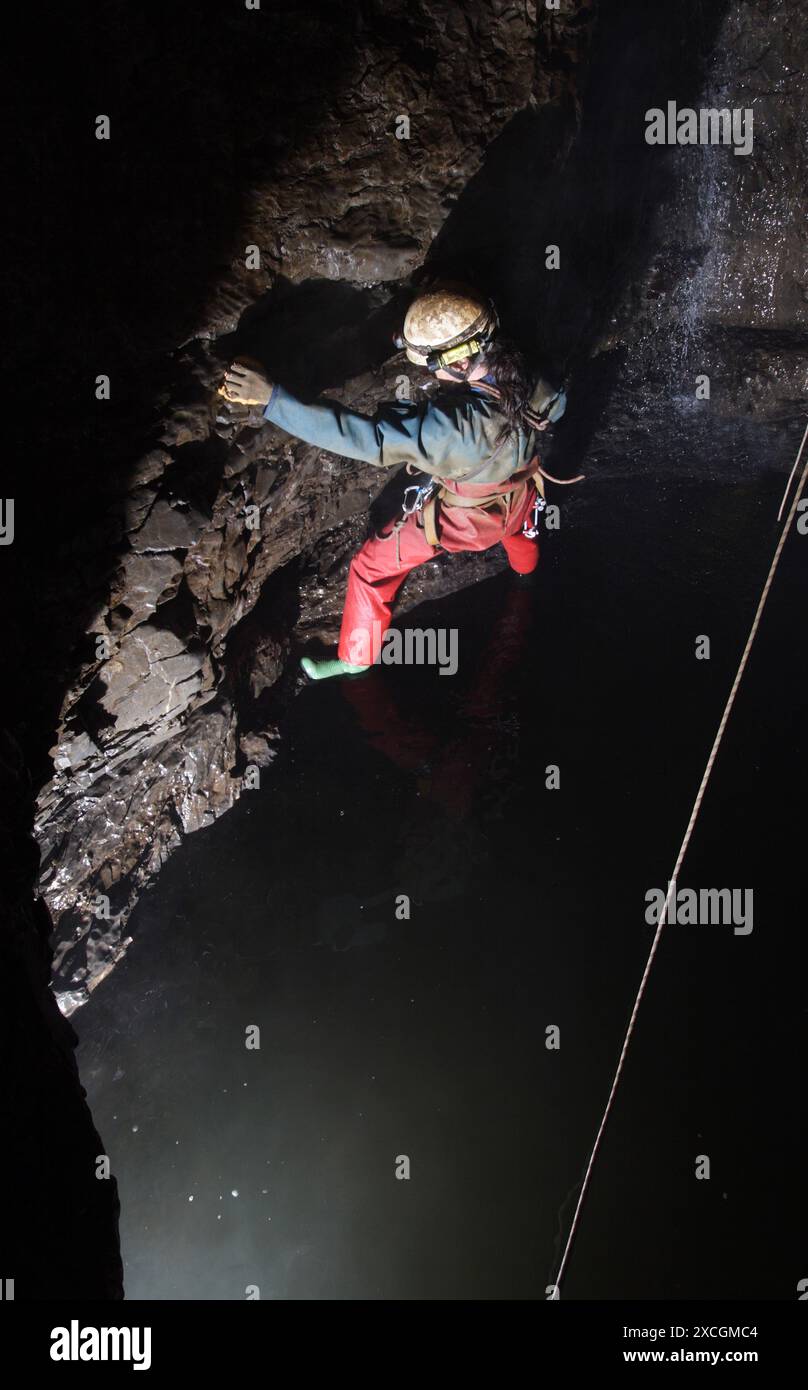 Cave explorer traverses across a ledge above a deep pool of water ...