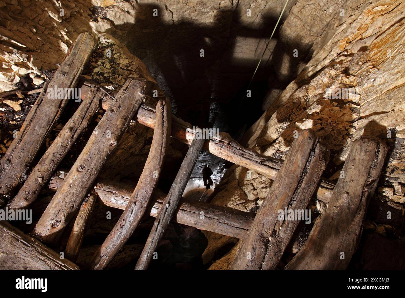A tiny black figure of a cave explorer ascends a rope climb through the ...