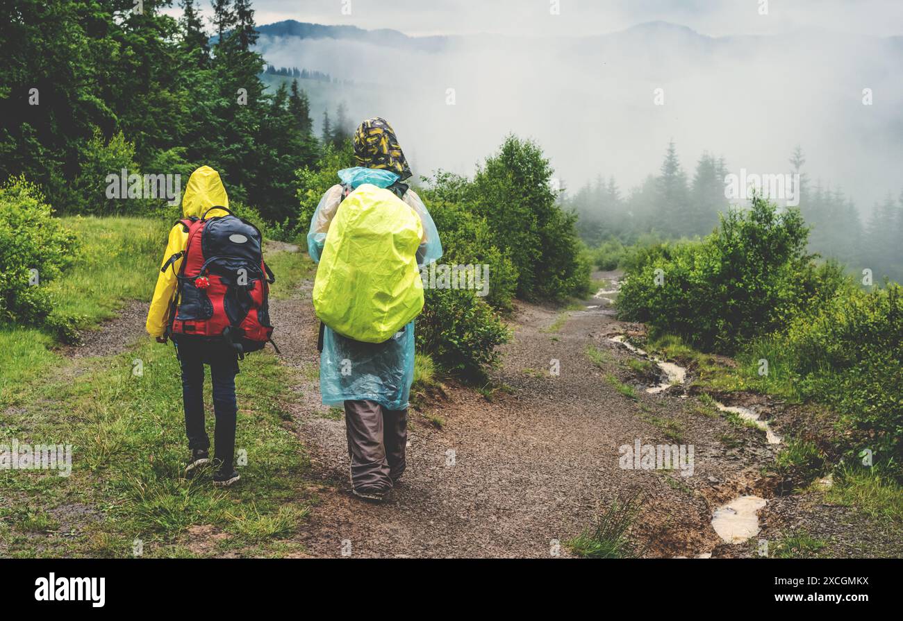 Two hikers tourist in raincoat walking on trail to green mountain ...