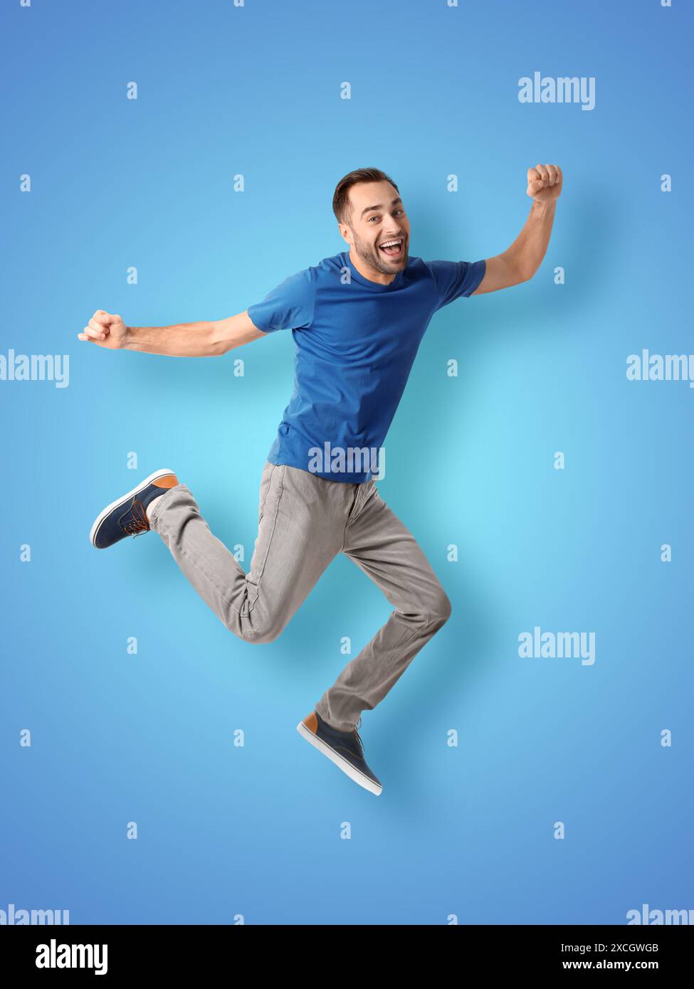 Positive young man jumping on light blue background Stock Photo - Alamy