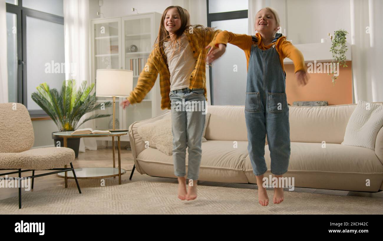 Two carefree Caucasian children little girls sisters laugh jumping ...