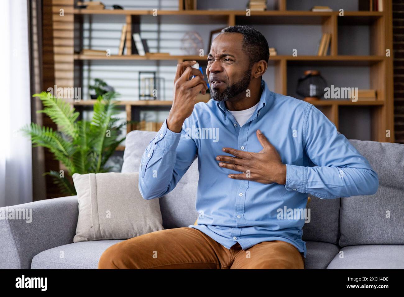 Man sitting on a couch using an asthma inhaler due to breathing ...