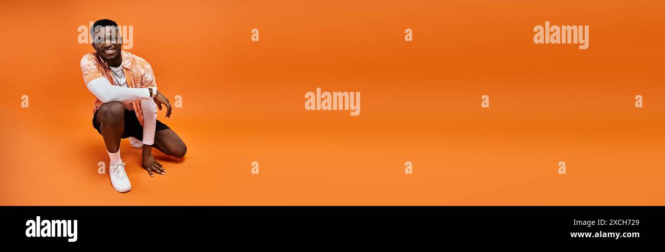 Fashionable African American man in stylish attire crouching on vibrant ...