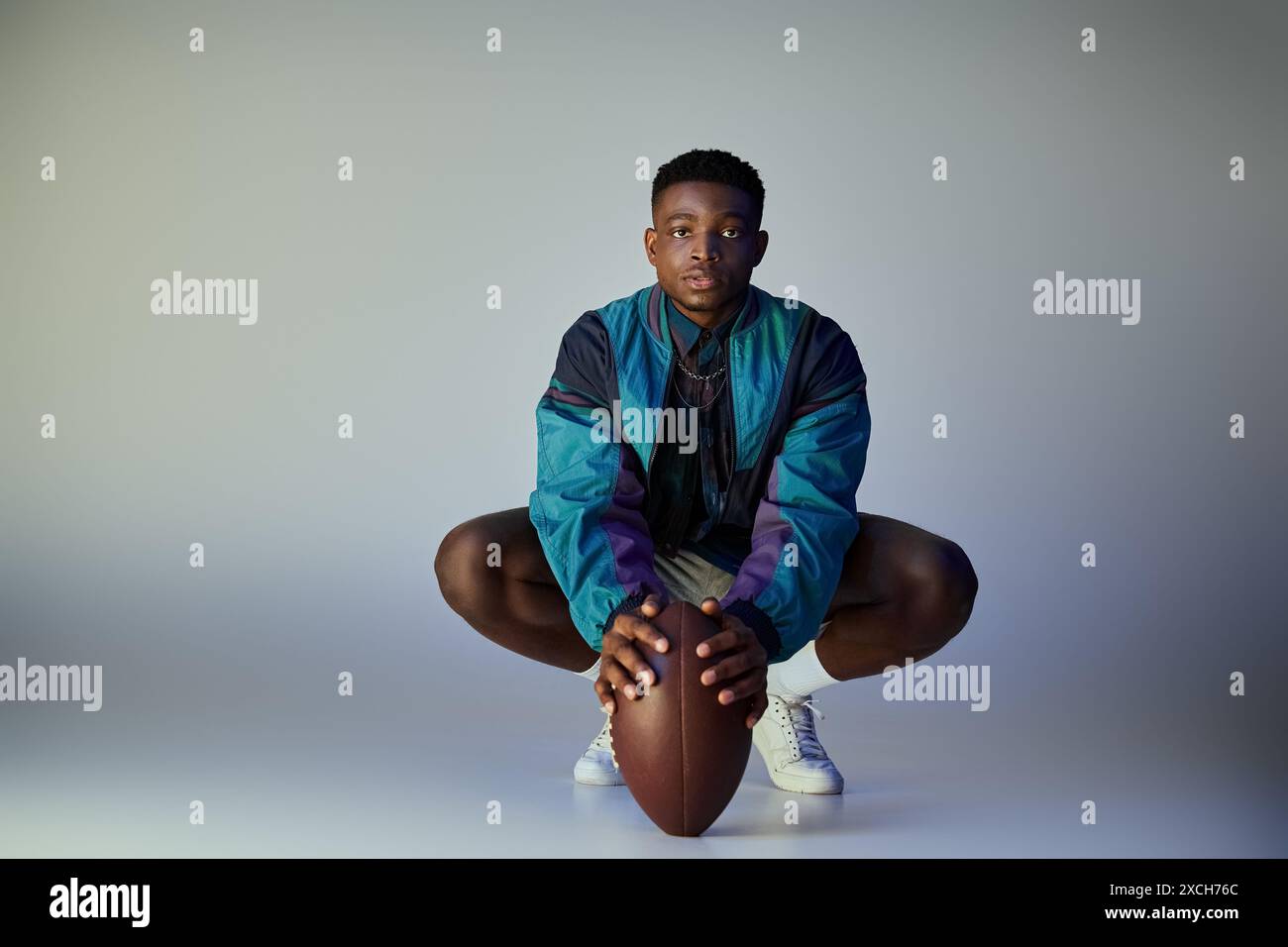 A stylish, athletic African American man crouching with a football ...